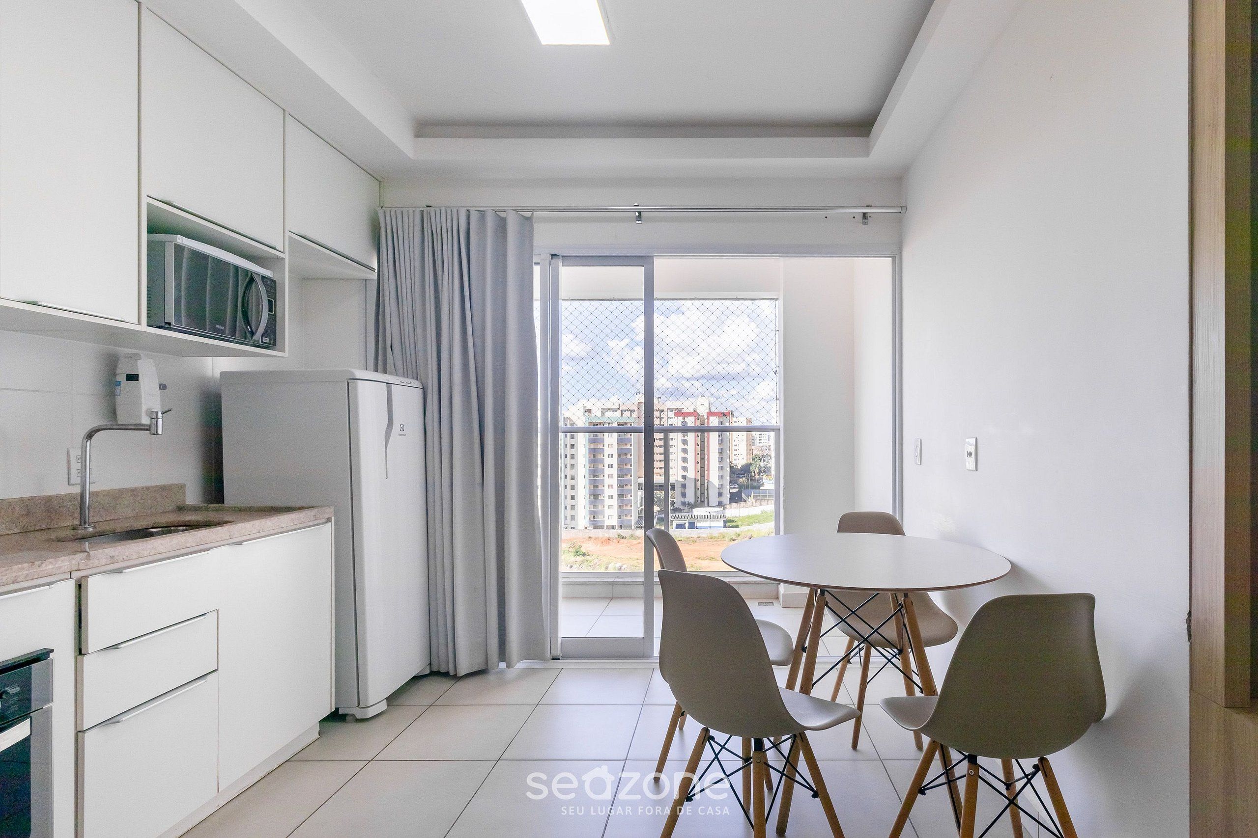 Uma cozinha moderna com micro-ondas embutido, geladeira e área de refeições com mesa redonda e quatro cadeiras.