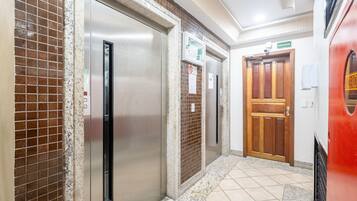 Área de elevadores com duas elevadoras, uma porta de madeira com a inscrição "GARAGEM" e piso revestido de azulejos.
