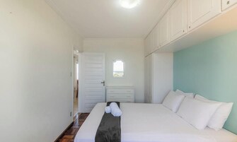 Quarto com cama, mesa de cabeceira, janela e porta.