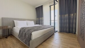 Quarto de hotel moderno com uma cama grande, mesa de cabeceira e vista para o mar através de uma varanda.