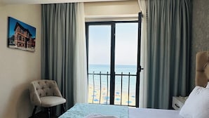 Quarto de hotel com uma cama, uma cadeira, um quadro e vista para a praia.