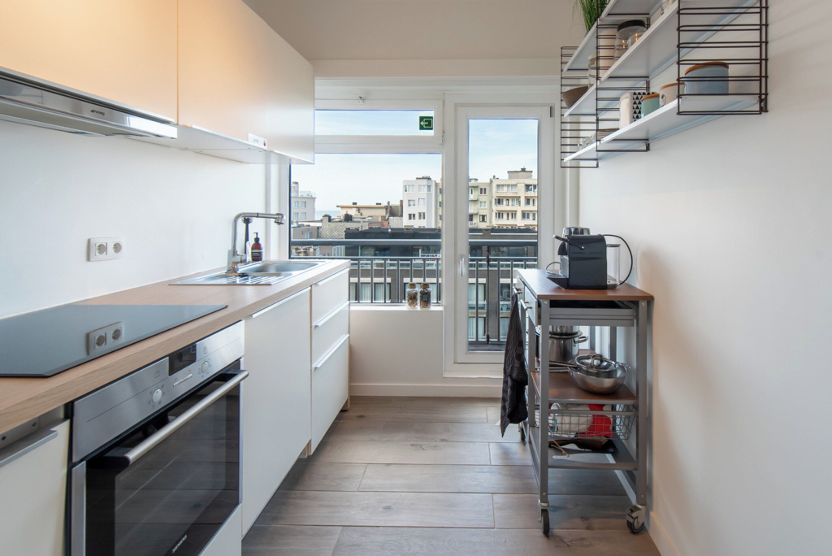 Cozinha estreita com forno embutido, pia e janela com vista para a paisagem urbana.