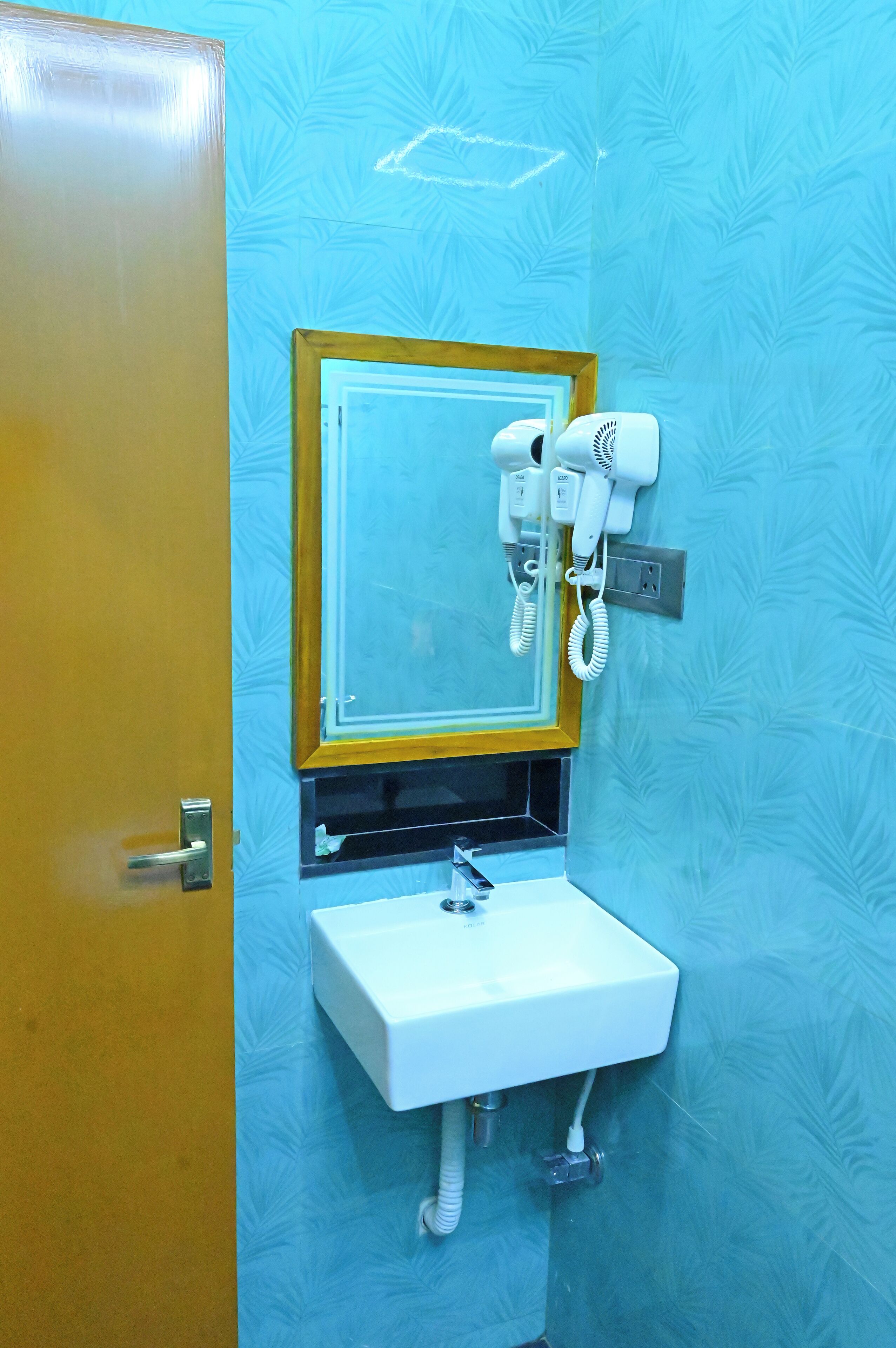 Casa de banho com lavatório, espelho e secador de cabelo fixado na parede.