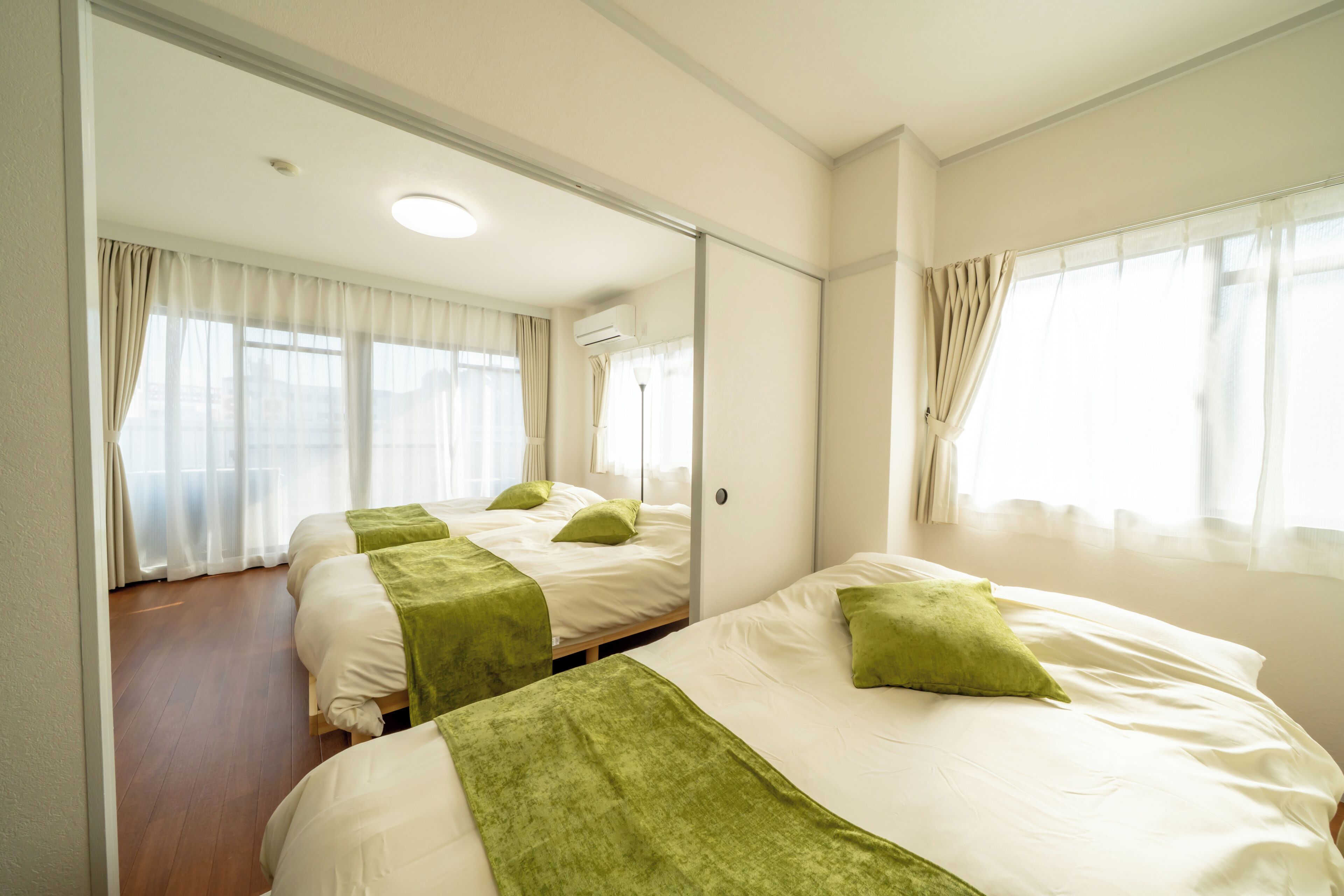 Quarto de hotel com duas camas, cada uma com colcha e travesseiro verde, um espelho grande e vista para a cidade pela janela.