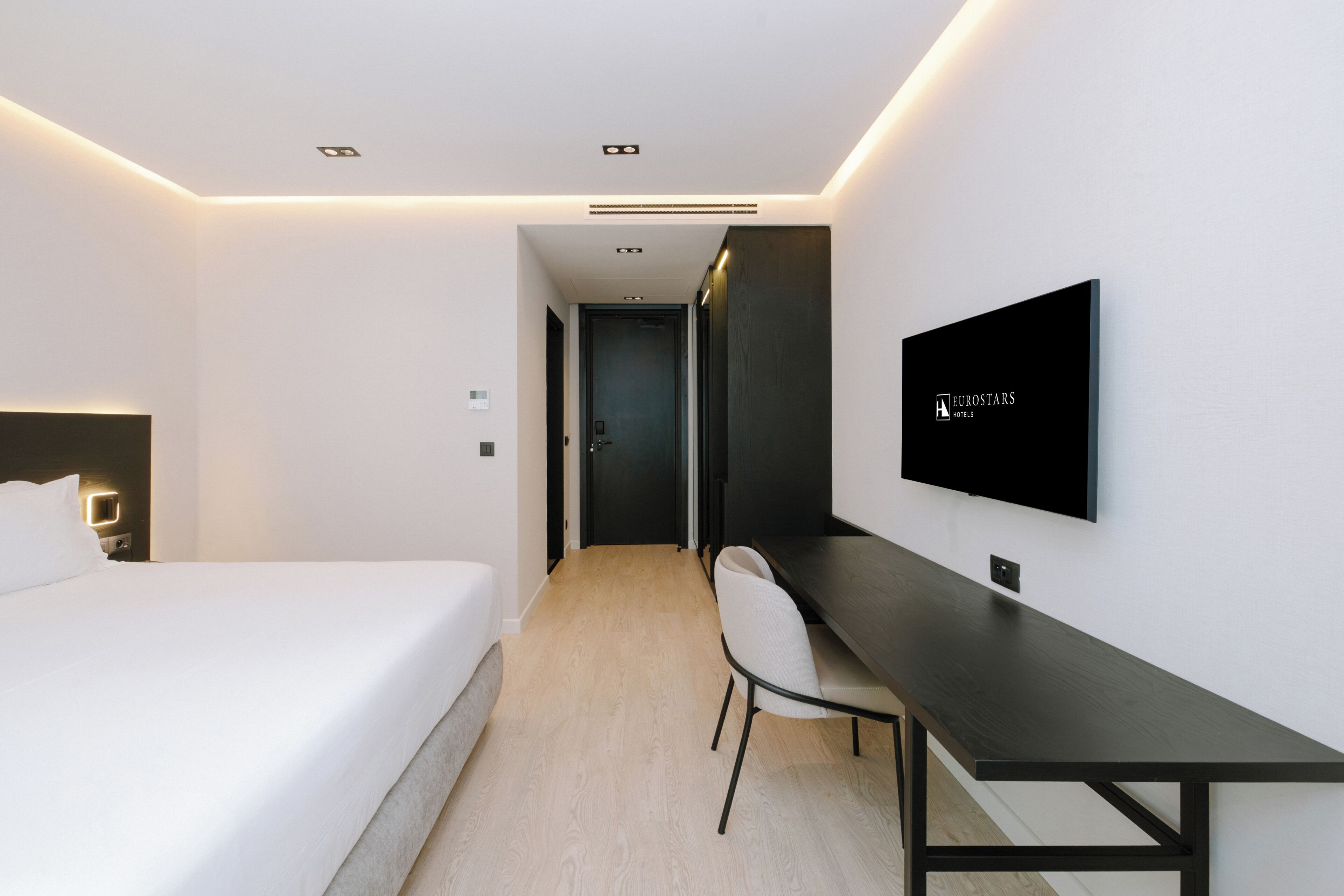 Quarto de hotel moderno com cama, escrivaninha, cadeira, televisão de tela plana e porta.