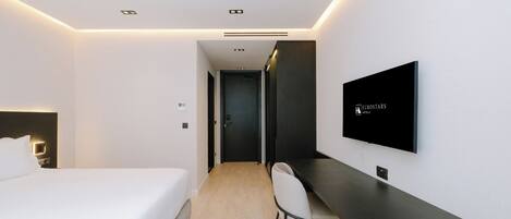 Quarto de hotel moderno com cama, escrivaninha, cadeira, televisão de tela plana e porta.