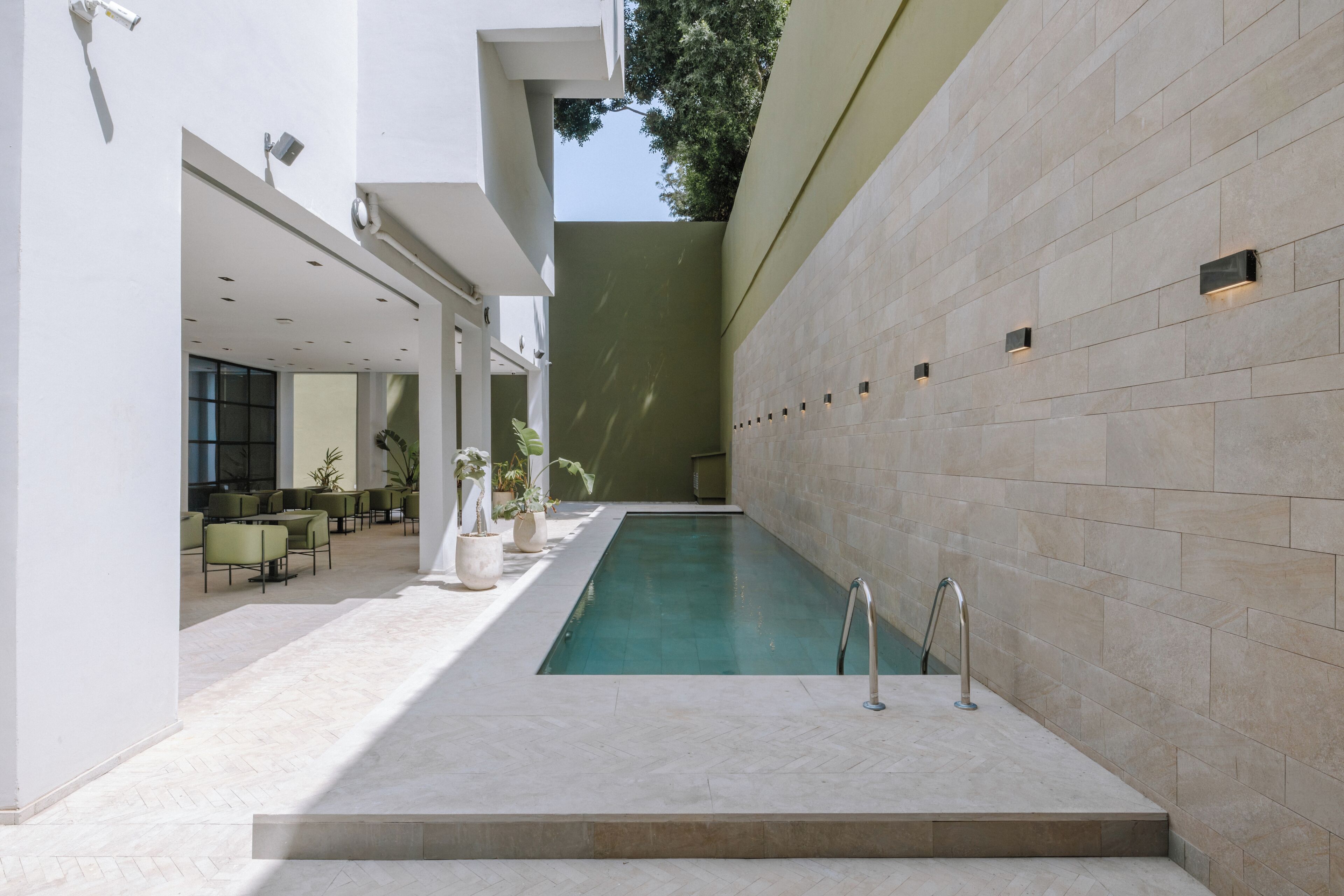 Uma área de piscina coberta moderna, com vista para o céu, envolta em design arquitetônico minimalista, com chão de azulejos e alguns vasos de plantas.