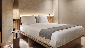 Quarto moderno com cama grande, cabeceira de madeira e iluminação ambiente.