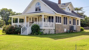 Uma casa de dois andares com varanda coberta, chaminé e gramado bem cuidado.