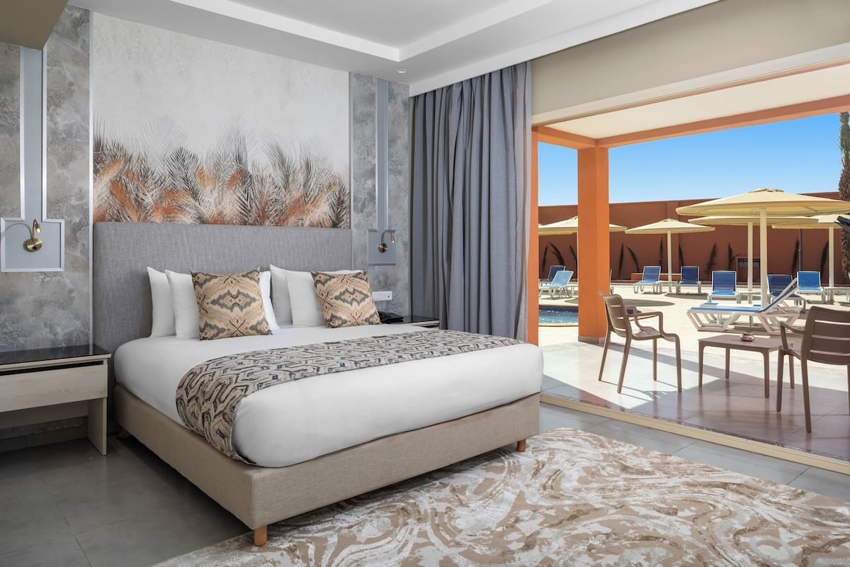 Quarto de hotel moderno com uma cama grande, vista para a área da piscina exterior e um grande quadro abstrato na parede.