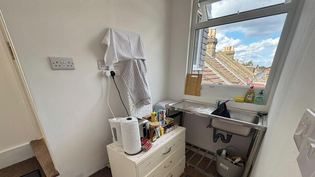 Cozinha compacta com janela, um varal, pia pequena e um armário com gavetas.