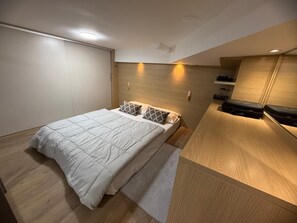 Quarto moderno com cama, cabeceira de madeira e espaço de armazenamento embutido.