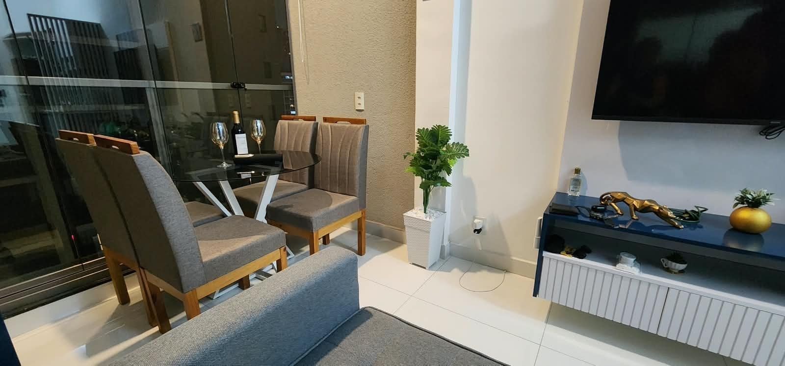Uma sala de estar moderna com divisória de vidro, área de estar, televisão e objetos decorativos.