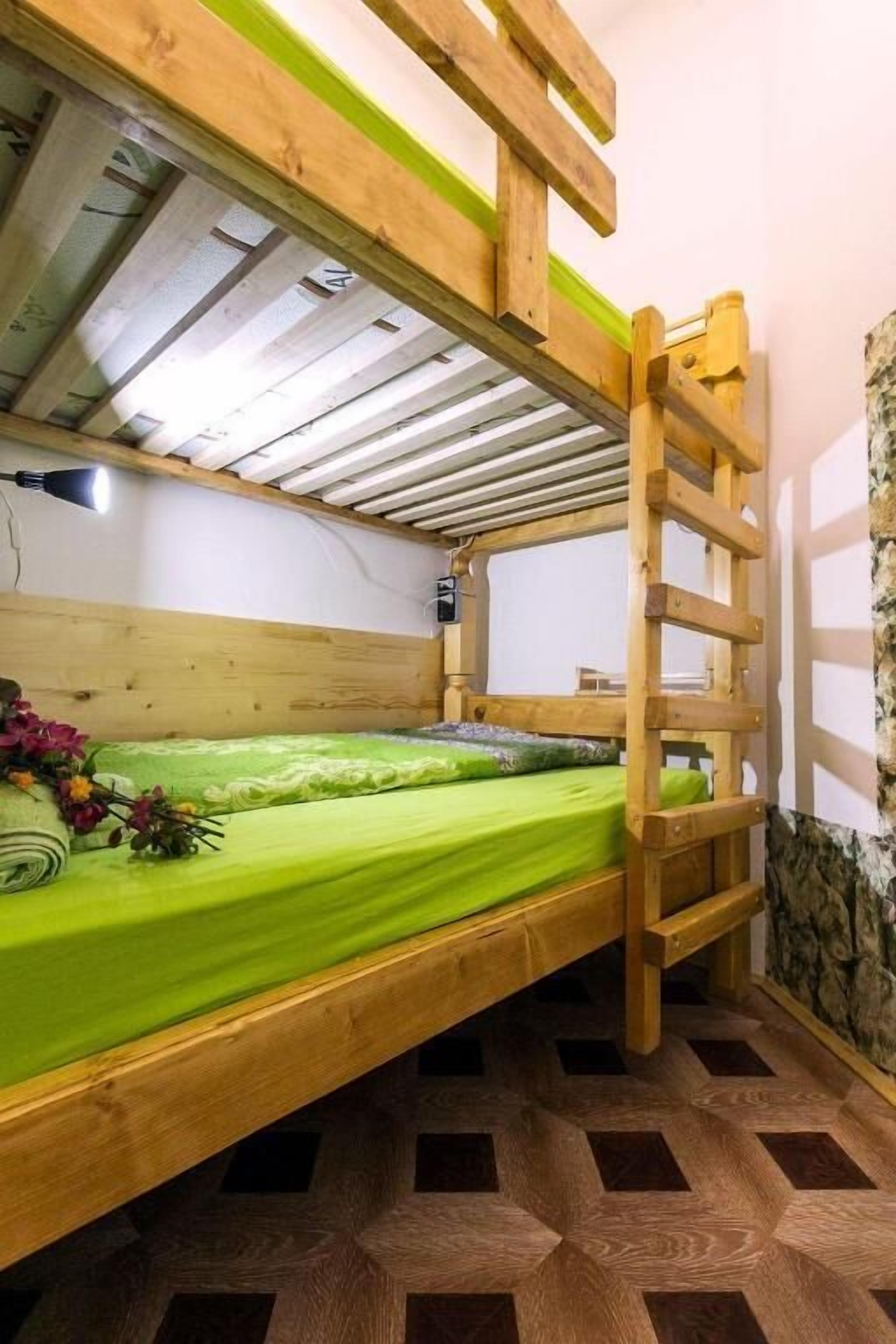 Uma cama beliche com escada de madeira, colcha verde e um arranjo floral no lado esquerdo.