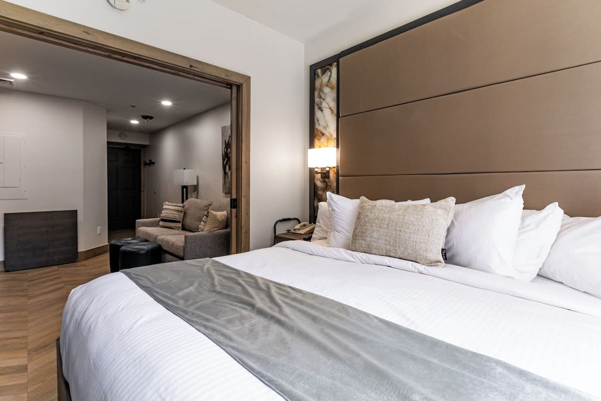 Quarto de hotel moderno com uma cama grande, um sofá, uma escrivaninha e um espelho.