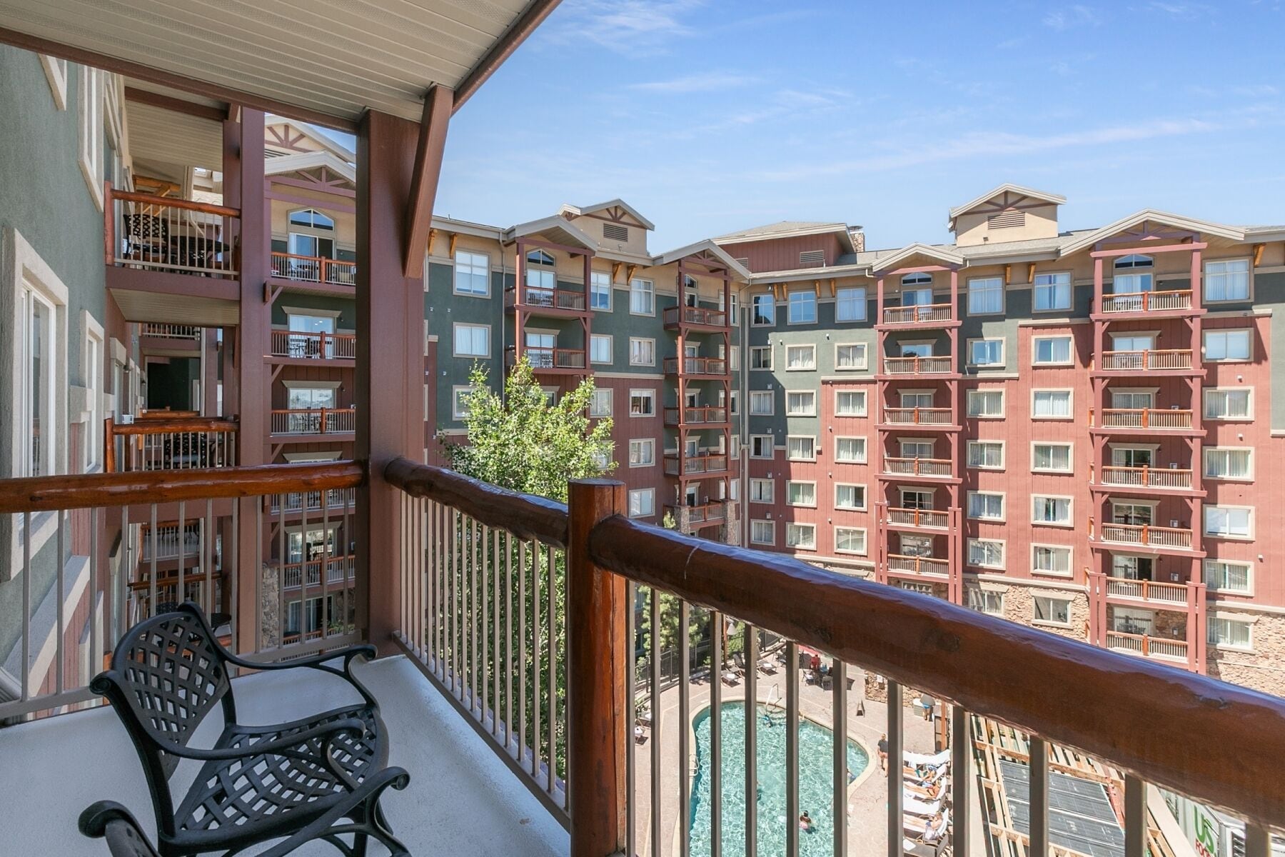 Uma varanda com vista para um prédio residencial, uma piscina e um céu claro.