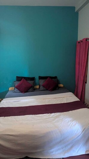Cama com colcha branca e avelã, duas almofadas e parede verde-água.