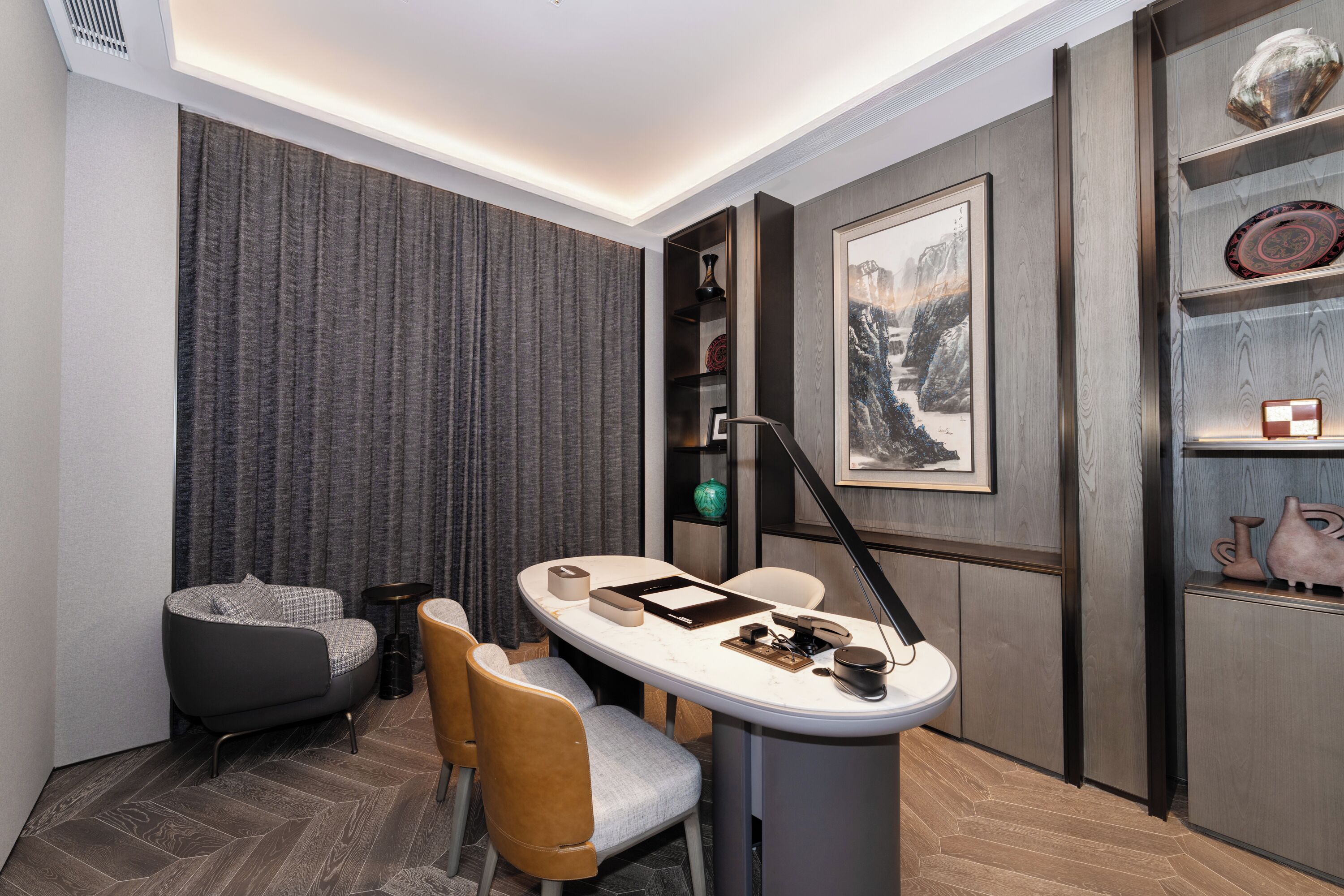 Quarto moderno com escrivaninha de mármore, duas cadeiras, estante e um quadro grande emoldurado na parede.