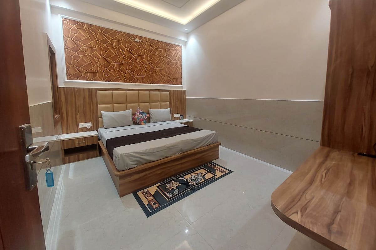 Quarto moderno com cabeceira de madeira, cama com roupa de cama branca, mesa de cabeceira e mesa lateral.