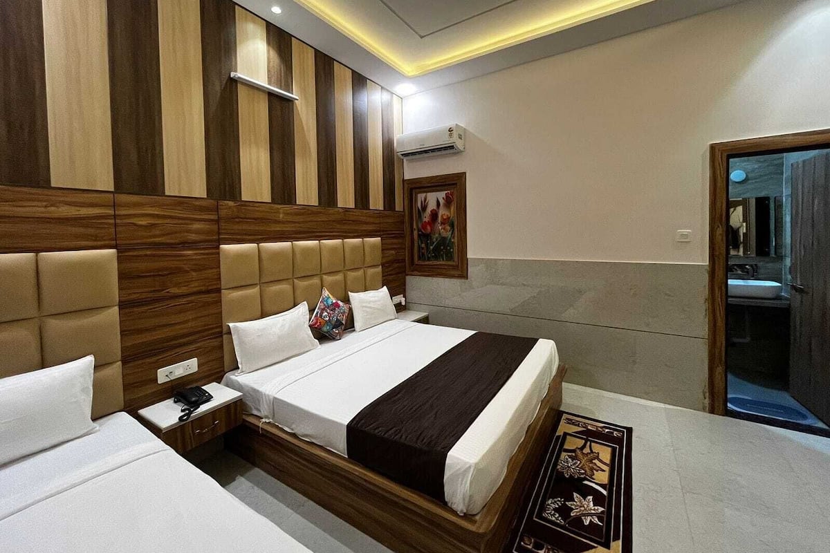 Quarto de hotel com uma cama grande, mesas de cabeceira, um ar condicionado fixado na parede e uma porta para o banheiro.