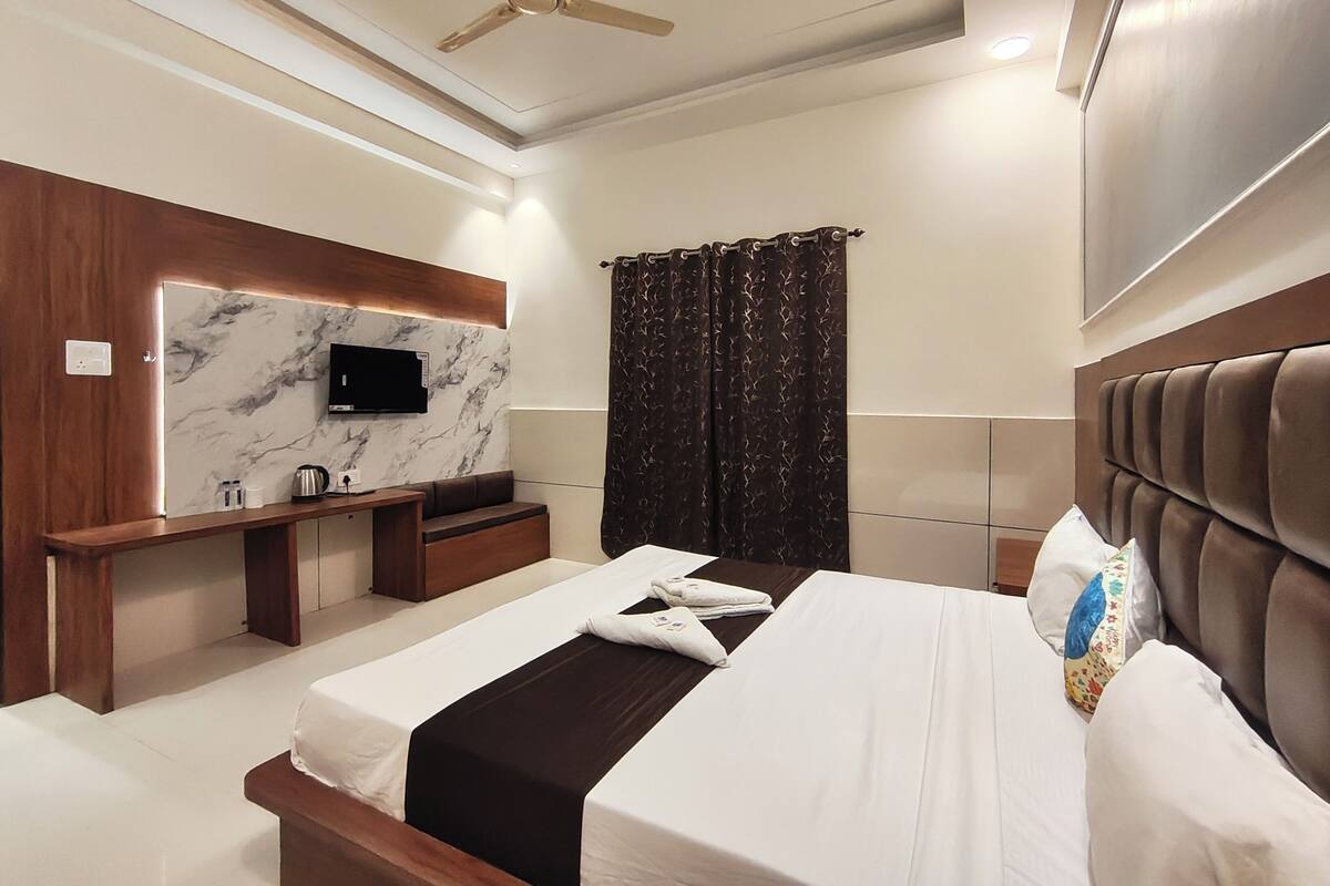 Quarto de hotel com cama, TV fixada na parede, ventilador de teto e janela com cortinas.