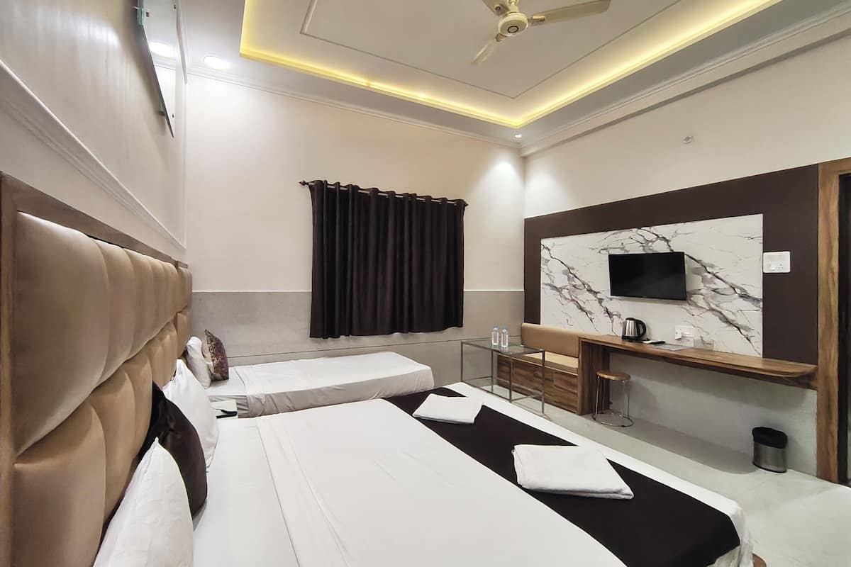 Quarto de hotel com duas camas, um ventilador de teto, uma TV fixada numa parede de mármore e uma pequena mesa com uma chaleira.
