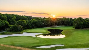 Um campo de golfe com bunkers de areia, lago e mastro de sinalização.