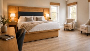 Quarto com uma cama grande, mesas de cabeceira com abajures, uma escrivaninha e duas poltronas.
