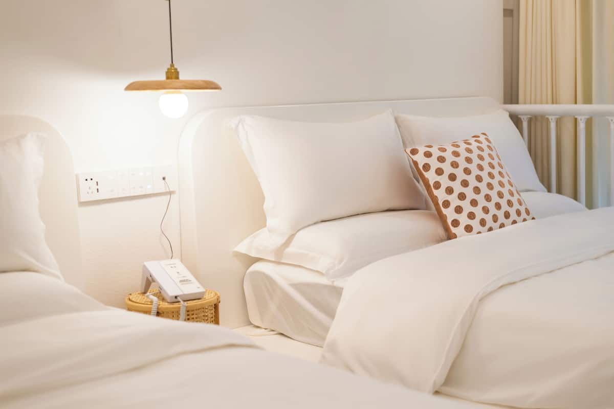Quarto com cama, mesa de cabeceira, abajur e tomada.