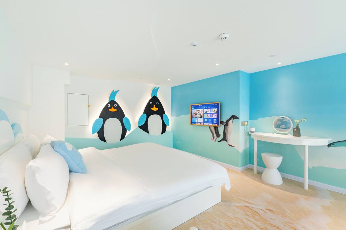 Quarto com cama, escrivaninha branca e parede decorada com pinguins.