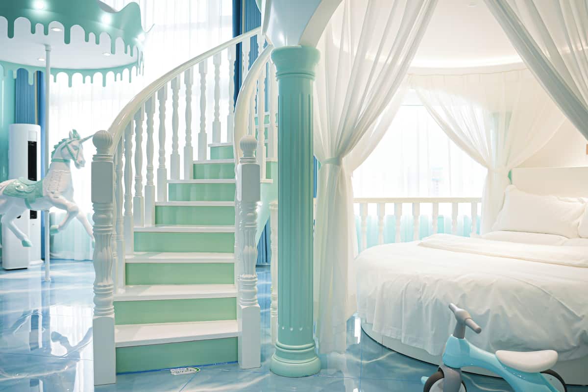 Quarto com cama, mesa de cabeceira e janela com cortinas.