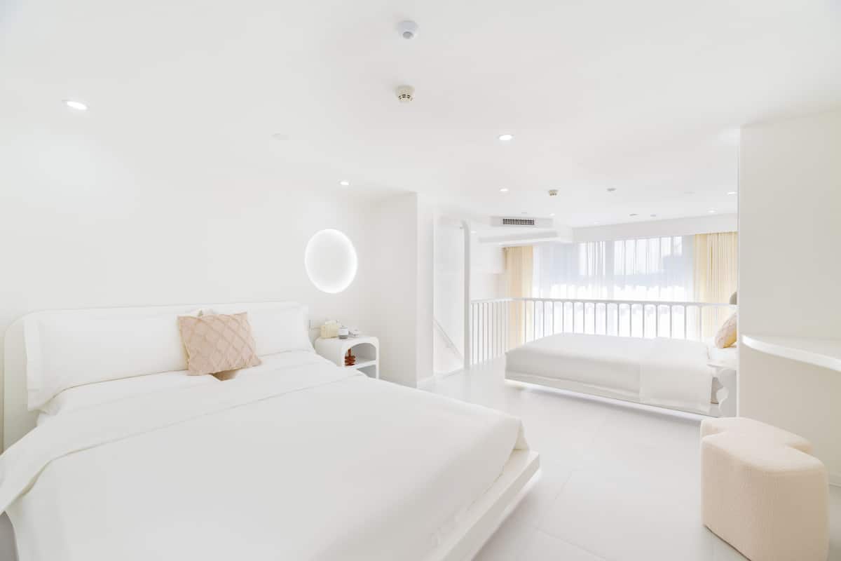 Quarto de hotel moderno com uma cama grande, um espaço de estar pequeno e uma varanda com guarda-corrimão.