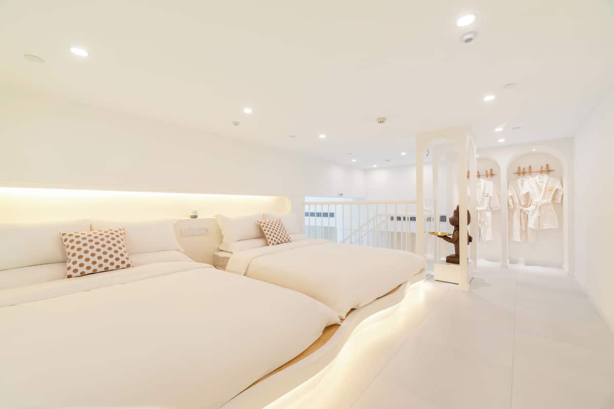 Quarto moderno com duas camas grandes, um guarda-roupa com roupas penduradas e uma pequena estátua.