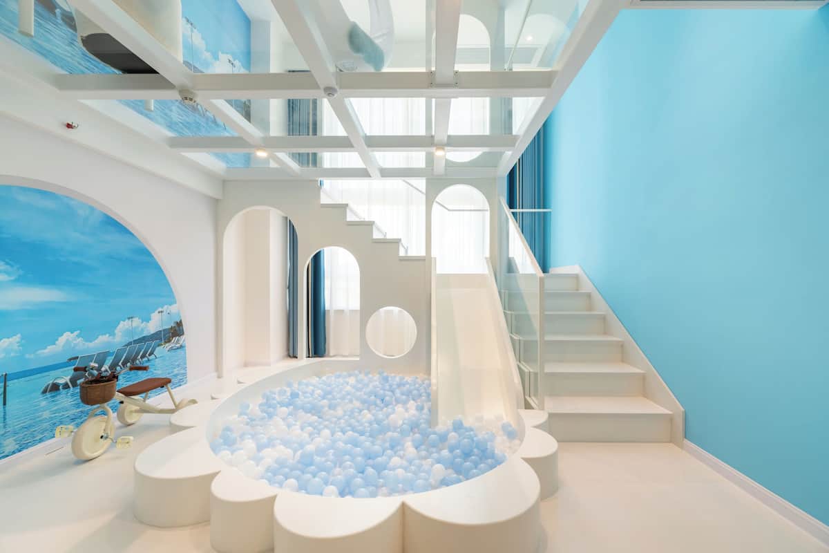 Decoração moderna com piscina de bolinhas, escada e um mural com paisagem de praia.