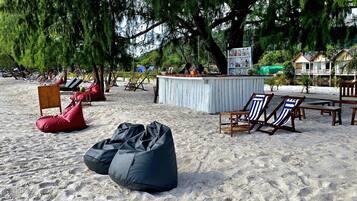 Uma área de relaxamento à beira-mar, com espreguiçadeiras, pufes e um bar.