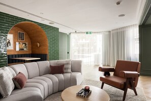 Um hall de hotel moderno com uma parede curva de madeira, um sofá, uma poltrona, uma mesinha e uma grande janela com cortinas.