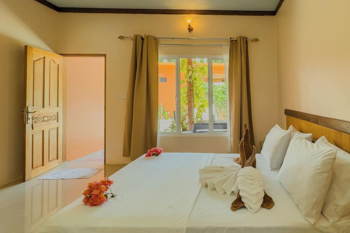 Quarto de hotel com cama, ventoinha no teto, janela com cortinas e vista para o exterior.
