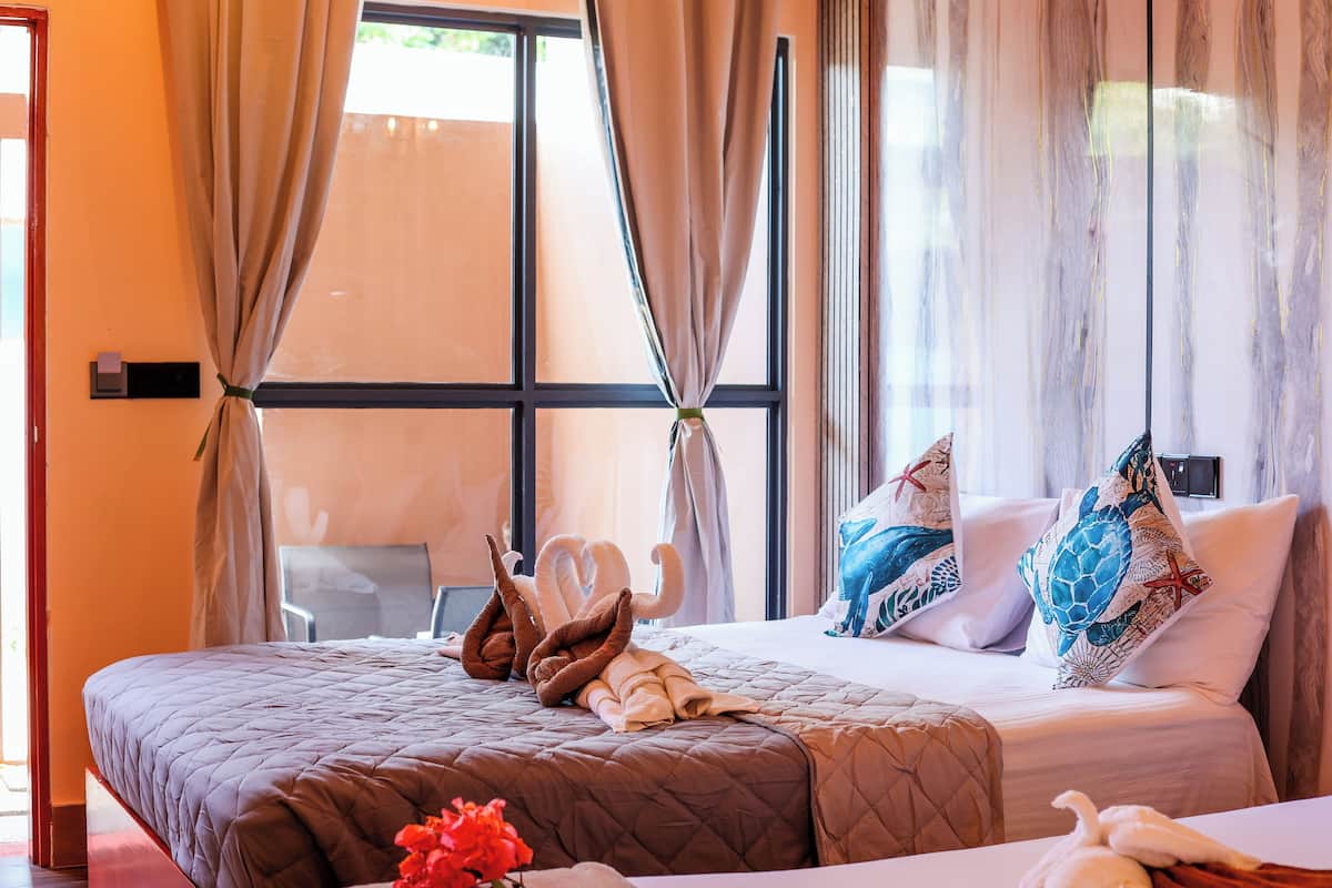 Quarto de hotel com cama, cortinas, janela e uma cadeira.
