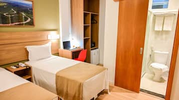 Quarto de hotel com uma cama, uma mesa com um laptop, uma cadeira vermelha, um mini frigorífico e área de duche.