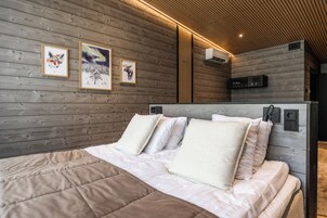 Quarto moderno com cabeceira de madeira, cama com roupa de cama branca e três obras de arte emolduradas na parede.
