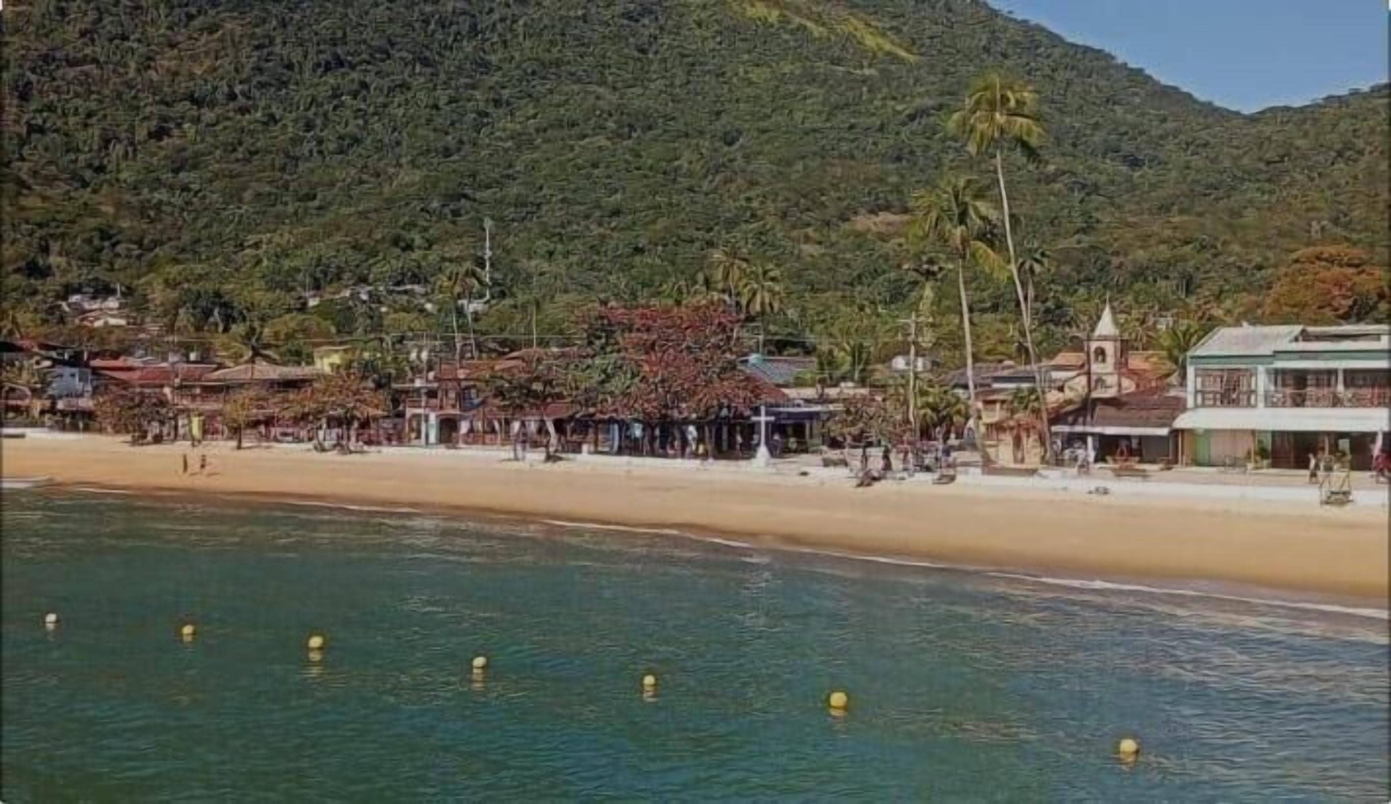 Uma praia com águas cristalinas, areia dourada e montanhas ao fundo.