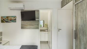 Quarto com cama, TV fixada na parede, quadro e porta de acesso a um banheiro.