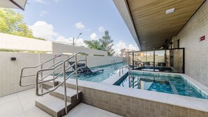 Piscina com degraus e vedação de vidro, rodeada por paredes revestidas de azulejos e teto de madeira.