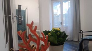 Um quarto com piso de concreto, uma planta em vaso, uma escultura de coral vermelho e uma cama com manta listrada.