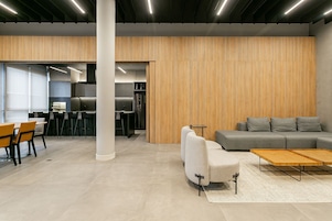 Um interior moderno com sofá cinzento, painéis de madeira e uma área de refeições com cadeiras e mesas.