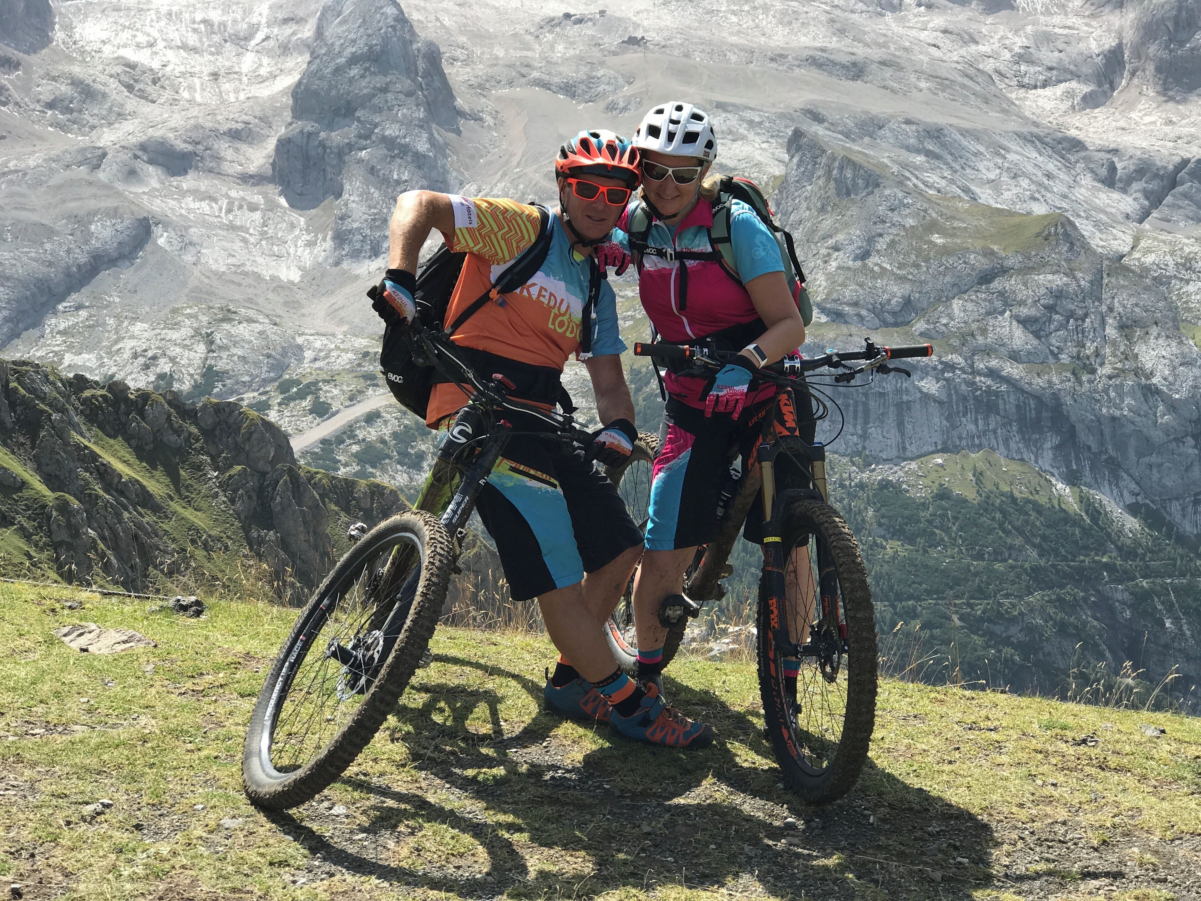 Duas pessoas em uma montanha com bicicletas, em meio a terreno rochoso e vegetação.