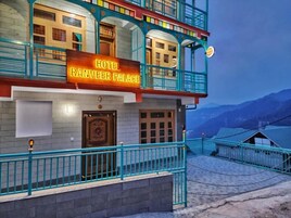 Um hotel chamado "Hotel Ranveer Palace", com uma placa visível, uma varanda com grades e vista para montanhas ao fundo.