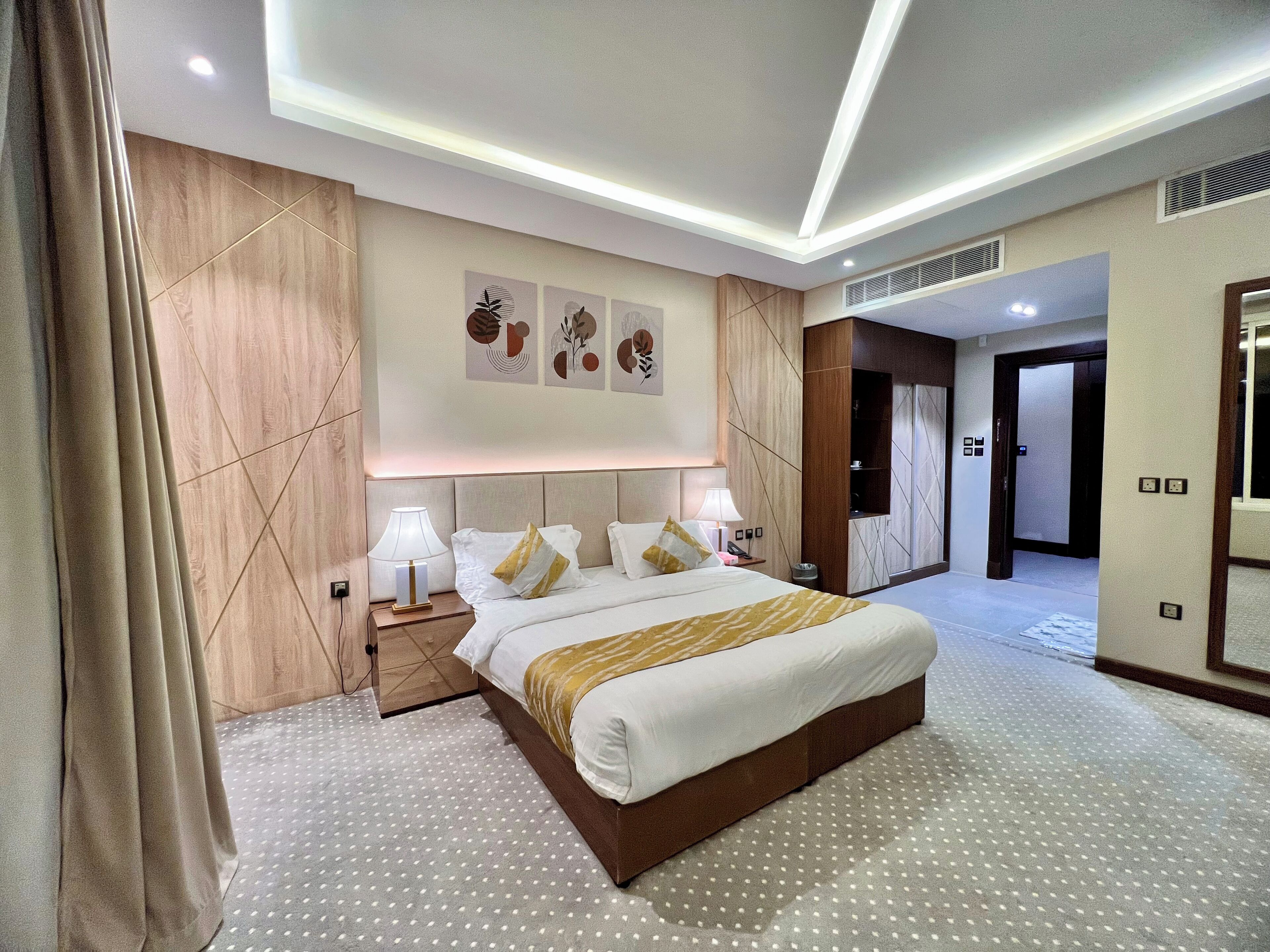 Quarto de hotel com uma cama grande, mesa de cabeceira, luminária, TV na parede e luz de teto.