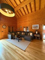 Interior acolhedor de uma cabana de madeira com um sofá seccional, uma mesa de centro e piso de madeira.