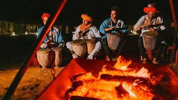 Quatro pessoas sentadas em volta de uma fogueira tocando tambores.